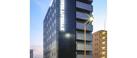 Um edifício moderno de hotel com uma placa chamativa 'HOTEL MAX', vários andares e uma entrada bem iluminada.