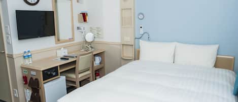 Quarto de hotel com cama, escrivaninha com computador, espelho, relógio e televisão fixada na parede.