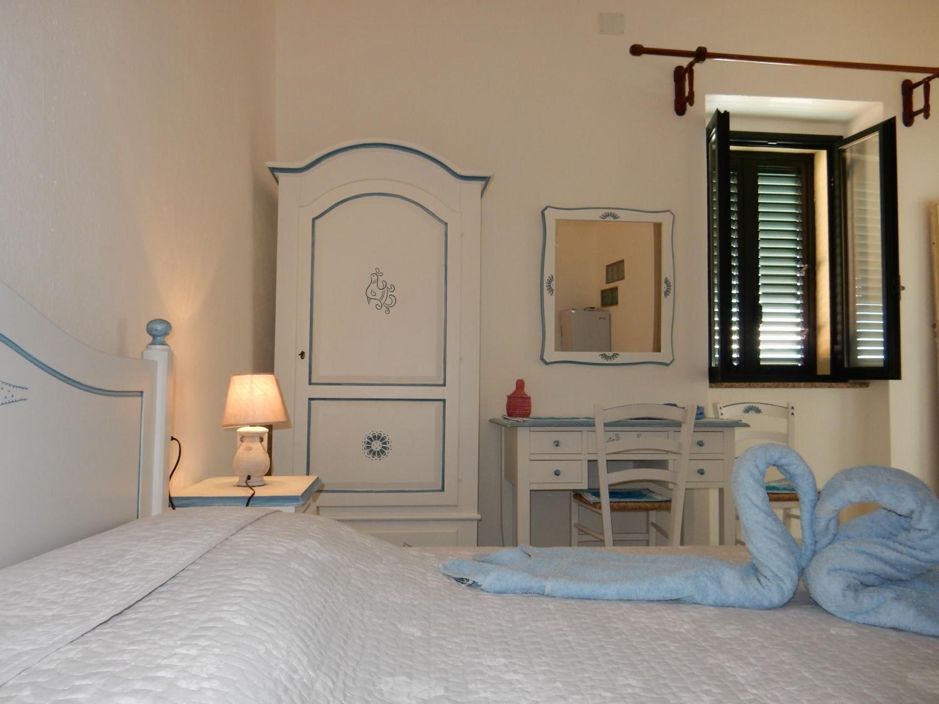 Quarto com cama, penteadeira, cadeira, escrivaninha, abajur, espelho e janela com persianas.