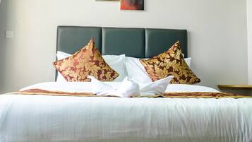 Cama bem arrumada com cabeceira verde, roupa de cama branca e almofadas estampadas.