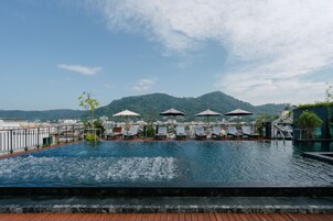 Piscina infinita no terraço com espreguiçadeiras e guarda-sóis, cercada por montanhas e vista da cidade.