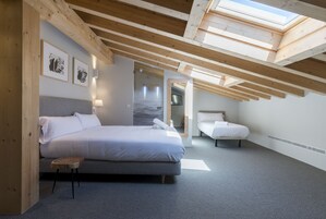 Quarto com claraboia, cama, mesa de cabeceira e abajur fixado na parede.