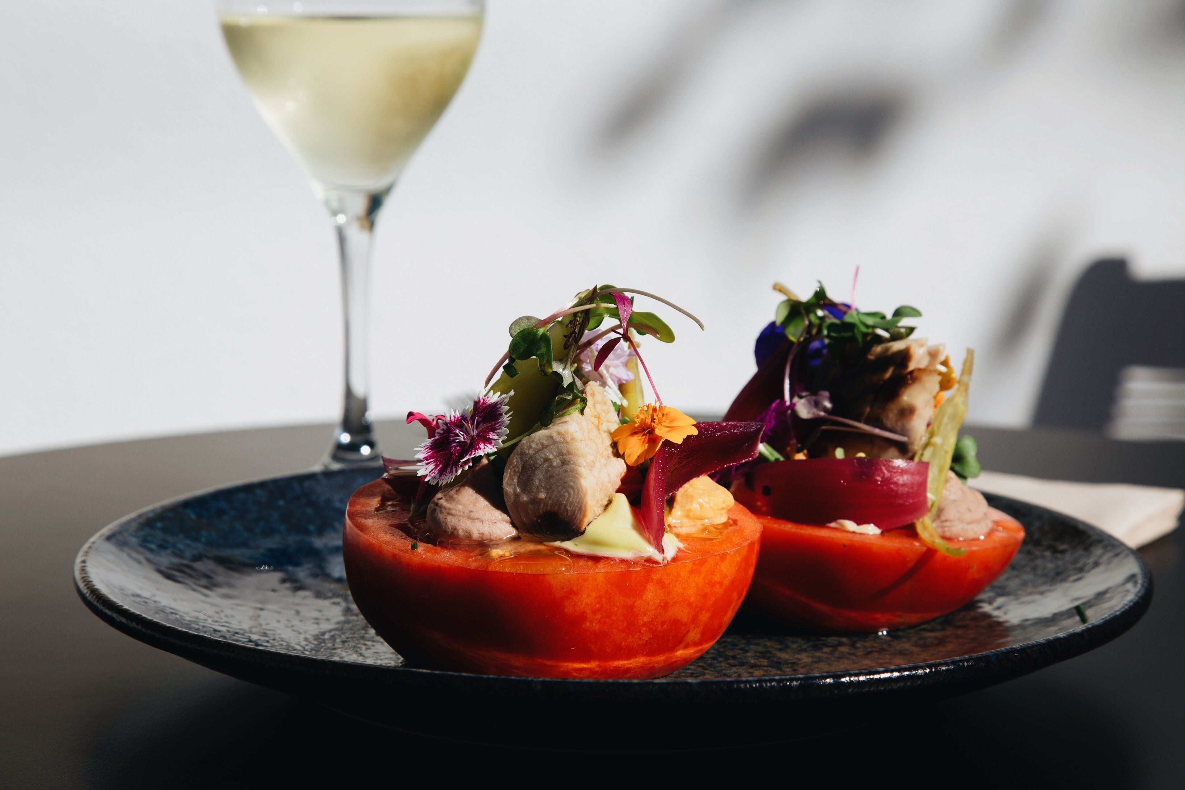 Um prato com dois tomates recheados e um copo de vinho branco.