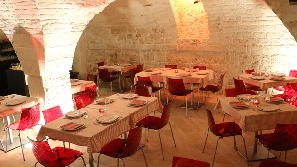 Um restaurante com mesas e cadeiras dispostas em formato semicircular, paredes de pedra e um teto alto e abobadado.