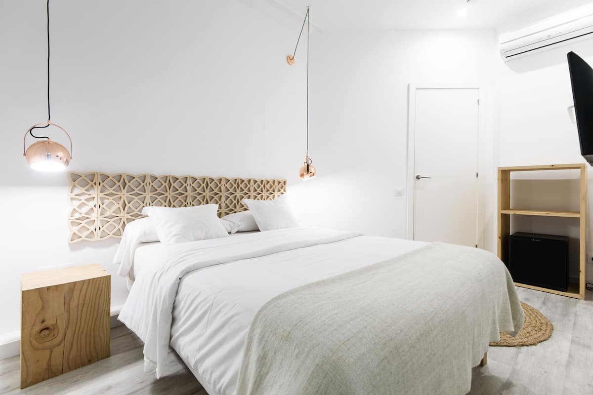 Quarto minimalista com cama, mesa de cabeceira de madeira, luminária pendente e estante embutida.