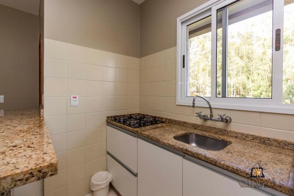 Cozinha com bancada de granito, pia de aço inoxidável e janela com vista para árvores.