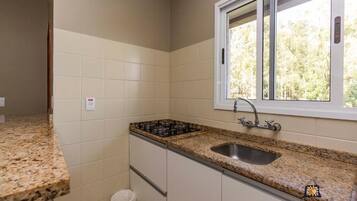 Cozinha com bancada de granito, pia de aço inoxidável e janela com vista para árvores.