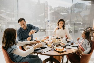 Uma família jantando à mesa com vista para a cidade, incluindo um copo de suco e diversos pratos.