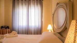 Quarto de hotel com uma cama bem arrumada, um espelho grande, uma luminária e vista para o exterior através das cortinas.