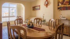 Uma sala de jantar com uma mesa redonda, cadeiras, um candelabro, um relógio e obras de arte nas paredes.