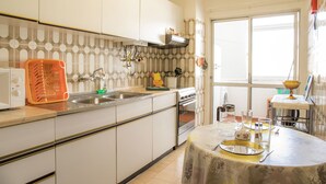 Cozinha com armários brancos, pia, fogão e área de jantar com mesa posta para dois.