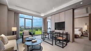 Quarto de hotel moderno com sofá, duas mesinhas, televisão e cama.