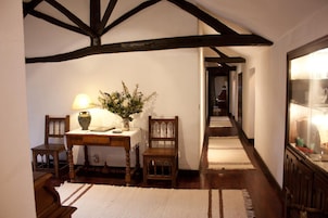 Um quarto acolhedor com vigas de madeira aparentes, uma mesa com um vaso e uma luminária, e uma cadeira.