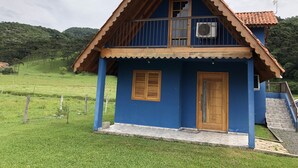 Uma casa de dois andares com varanda, venezianas de madeira e telhado de telhas.