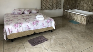 Quarto com cama, banheiro com banheira e janela com cortinas.