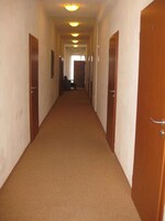 Um corredor comprido e estreito com pisos cobertos de carpete e portas de madeira em ambos os lados.