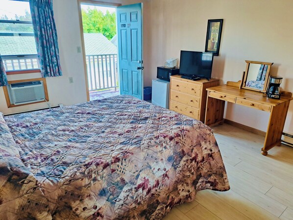 Quarto com uma cama, escrivaninha, televisão e porta para área externa.