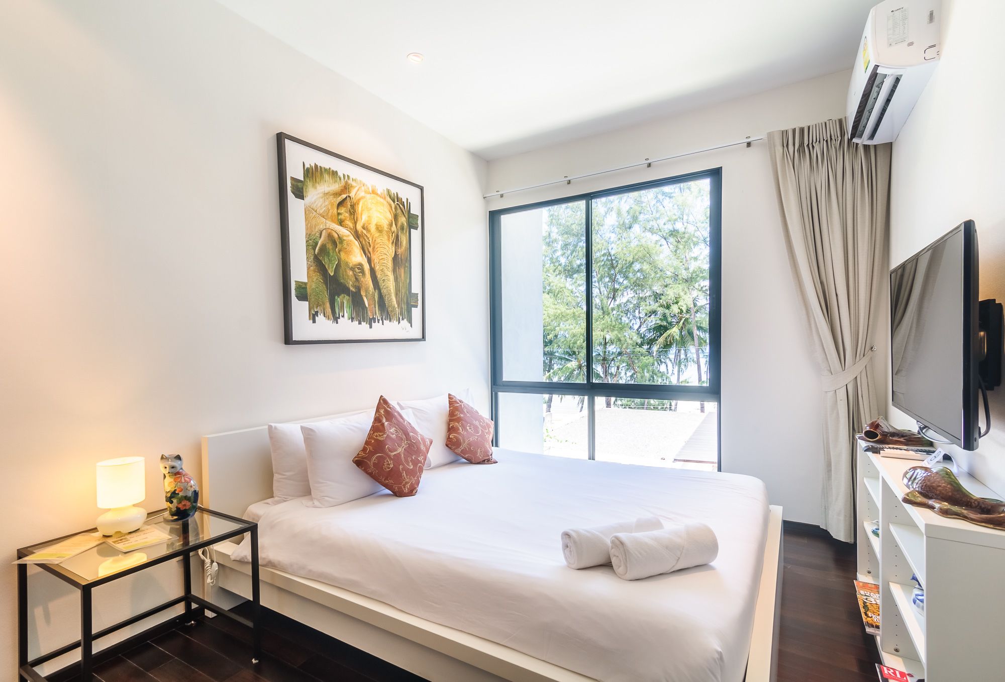 Quarto de hotel com uma cama grande, uma mesa de cabeceira, uma televisão e uma janela com cortinas.