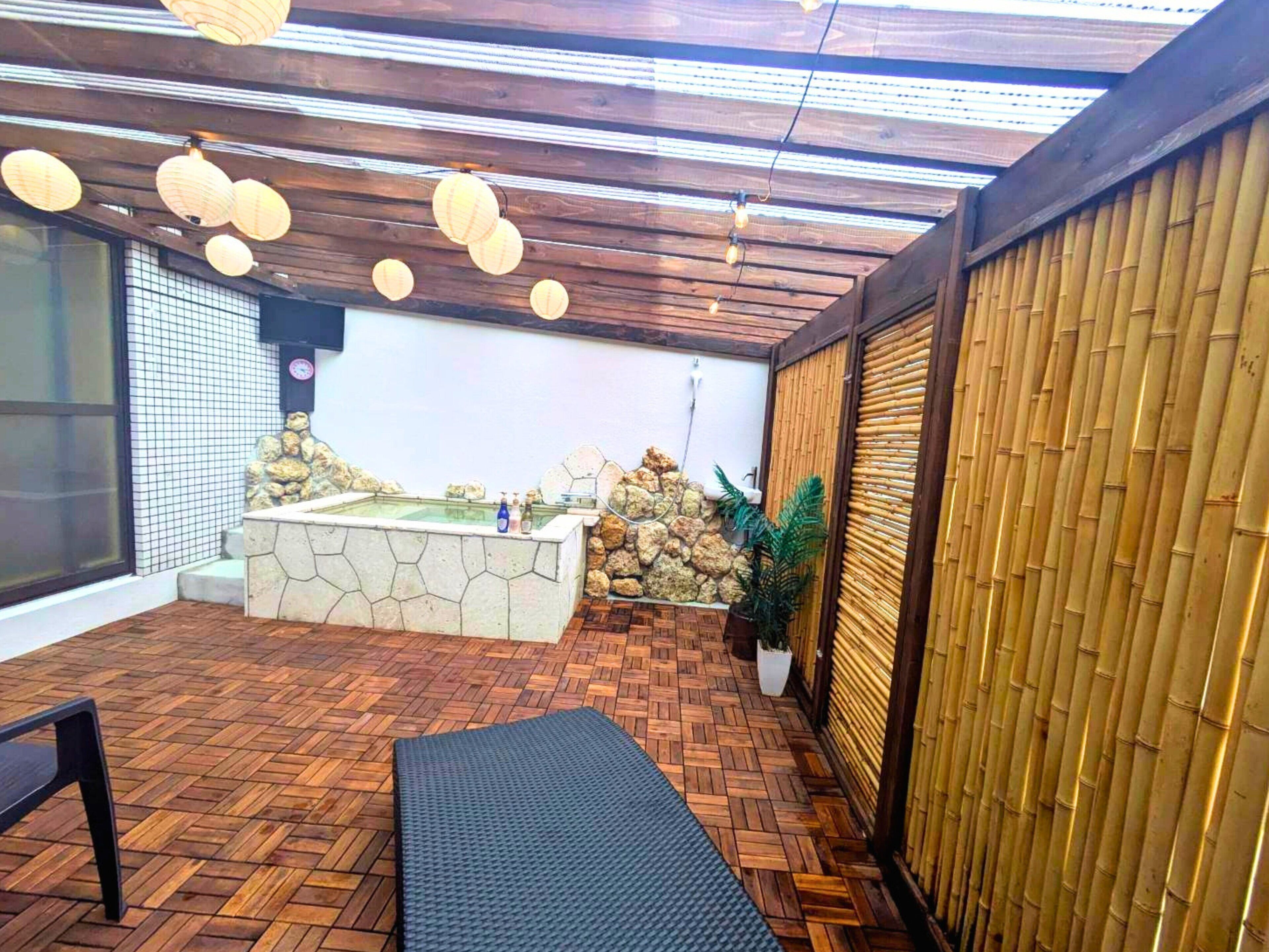 Uma área de spa com uma banheira de pedra quente, piso de madeira e parede de bambu.