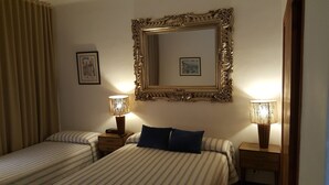 Quarto de hotel com duas camas de solteiro, um espelho grande e decorativo, e duas luminárias de cabeceira.