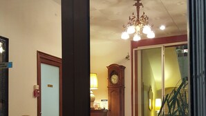 Quarto com uma cadeira de madeira, uma planta grande em vaso, um relógio e um candelabro.