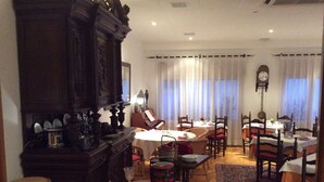 Uma área de refeições com um grande armário de madeira, várias mesas de jantar, cadeiras e um tapete estampado.