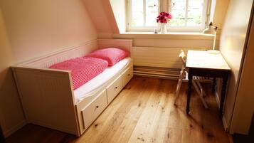 Um quarto pequeno e acolhedor com uma cama de solteiro, uma mesa de estudo e uma janela com vista.