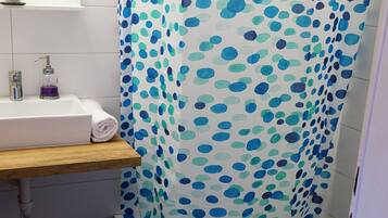 Um banheiro com cortina de chuveiro estampada em bolinhas azuis e brancas, pia branca com dispensador de sabonete e vaso sanitário.