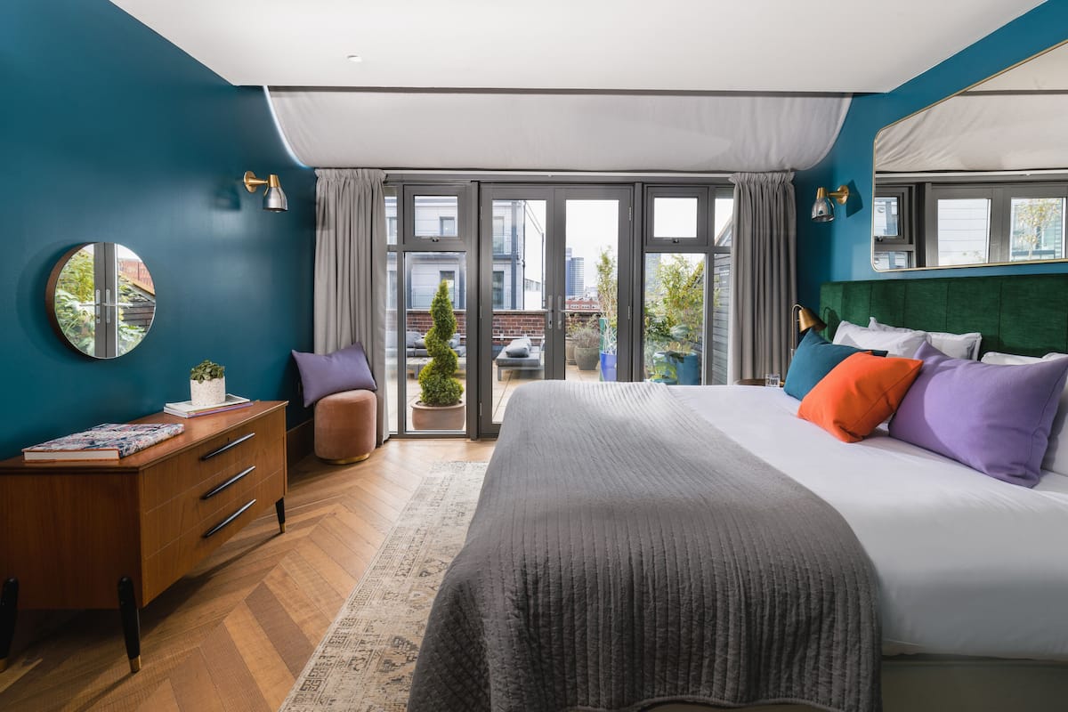 Quarto com cama grande, cômoda, espelho redondo e vista para o exterior através de uma porta de correr.