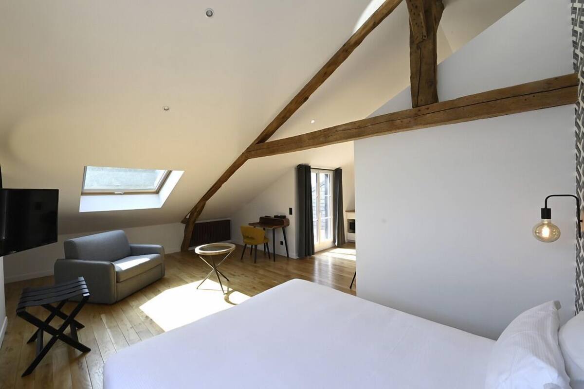 Quarto de loft moderno com teto inclinado, claraboia, cama, sofá, mesa pequena e televisão.