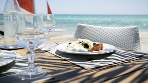 Mesa com prato de comida, dois copos e uma garrafa em um cenário de praia.