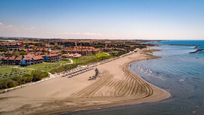 Um resort costeiro com vários edifícios, uma praia de areia e vista para o mar.