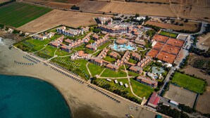 Vista aérea de um resort à beira-mar, com vários edifícios, uma praia e uma piscina grande.