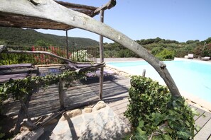 Um deck de madeira com cadeiras de descanso, piscina e vista para uma paisagem montanhosa.
