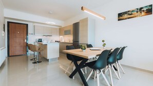 Uma cozinha moderna com uma ilha central, uma área de refeições com mesa de madeira e cadeiras pretas, e uma obra de arte na parede retratando uma cena de praia.