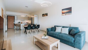 Uma sala de estar moderna com um sofá azul, uma mesa de centro de madeira e uma área de jantar com cadeiras e uma mesa.