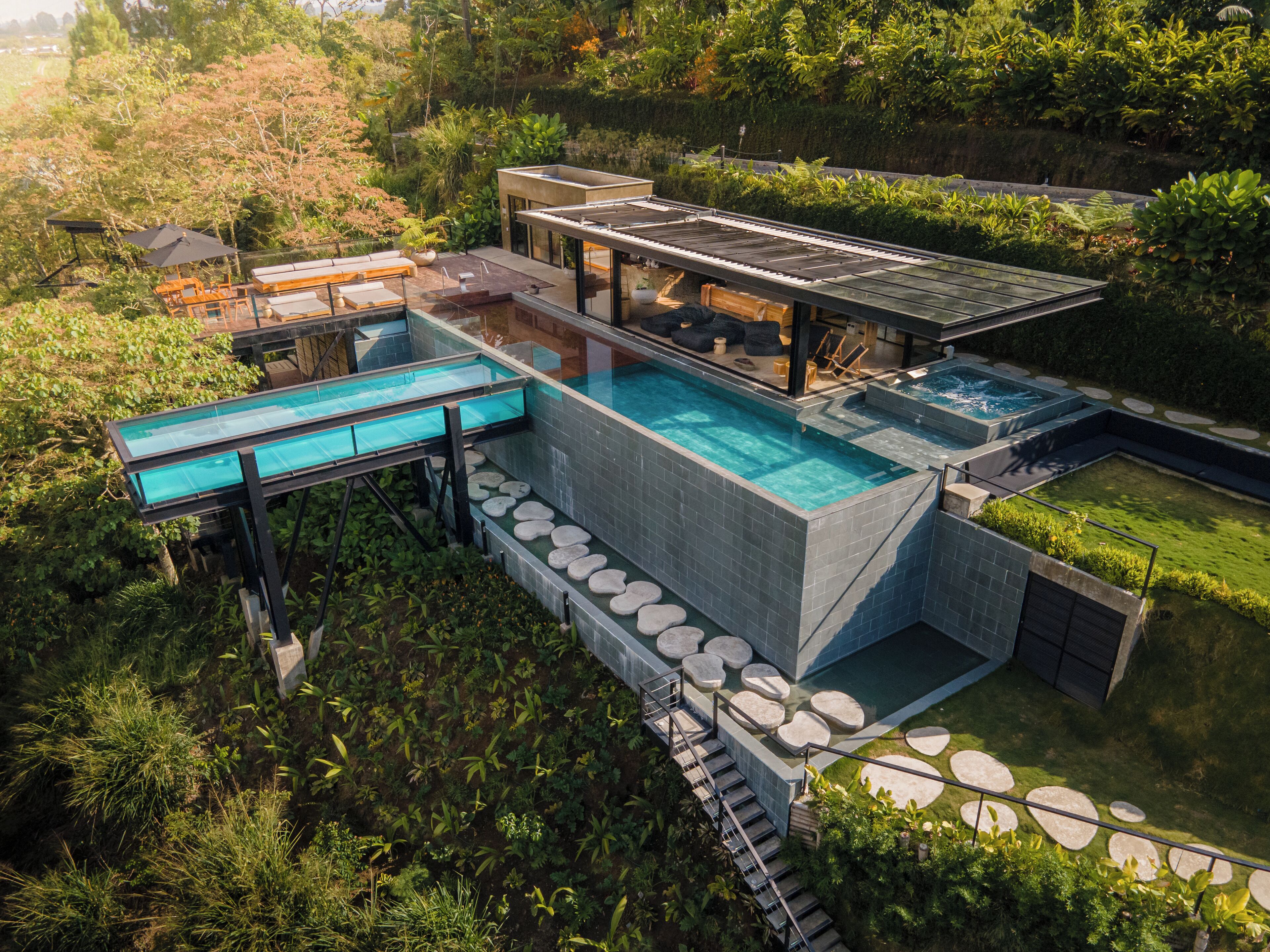Uma casa moderna com uma grande piscina, área de estar externa e uma ponte de vidro.