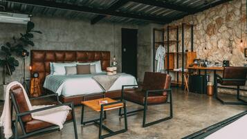 Quarto moderno com uma cama grande, área de estar com uma mesa de centro e uma parede de pedra.