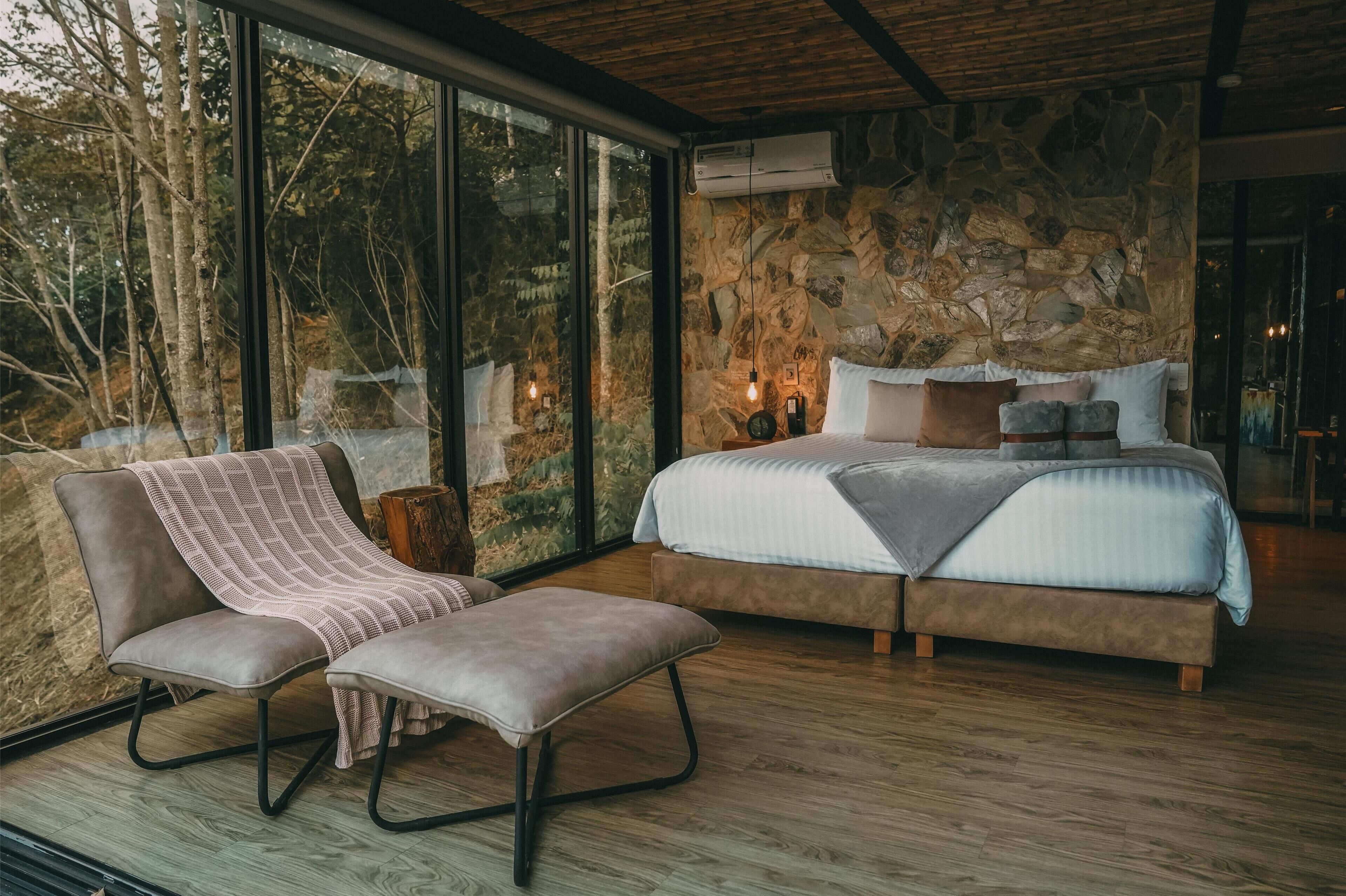 Quarto com cama grande, chaise longue e parede de pedra.