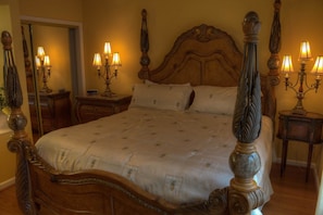 Uma cama com dossel adornada por um cobre-leito estampado com motivos florais, com cabeceiras e peseiras de madeira ornamentada.