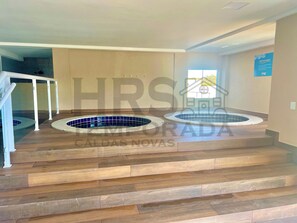 Uma área de piscina com duas banheiras de hidromassagem, piso de madeira e uma escadaria para um andar superior.