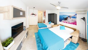 Quarto de hotel moderno com uma cama grande, televisão, ventilador de teto e uma pintura representando uma paisagem costeira.