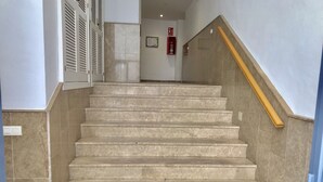 Um conjunto de degraus de mármore bege com um corrimão de madeira, conduzindo a um patamar.