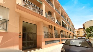 Um edifício residencial com vários andares, varandas, portão fechado e um carro estacionado.