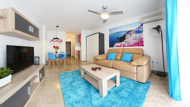 Uma sala de estar moderna com um sofá bege, uma mesa de centro, uma televisão e um tapete azul.