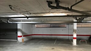 Uma garagem de estacionamento com pisos de concreto, dutos de ventilação e vagas numeradas.