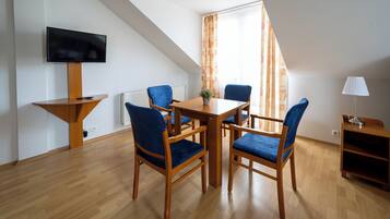 Uma sala de estar moderna com uma mesa de madeira, cadeiras azuis, uma televisão de tela plana, uma luminária e uma janela com cortinas.