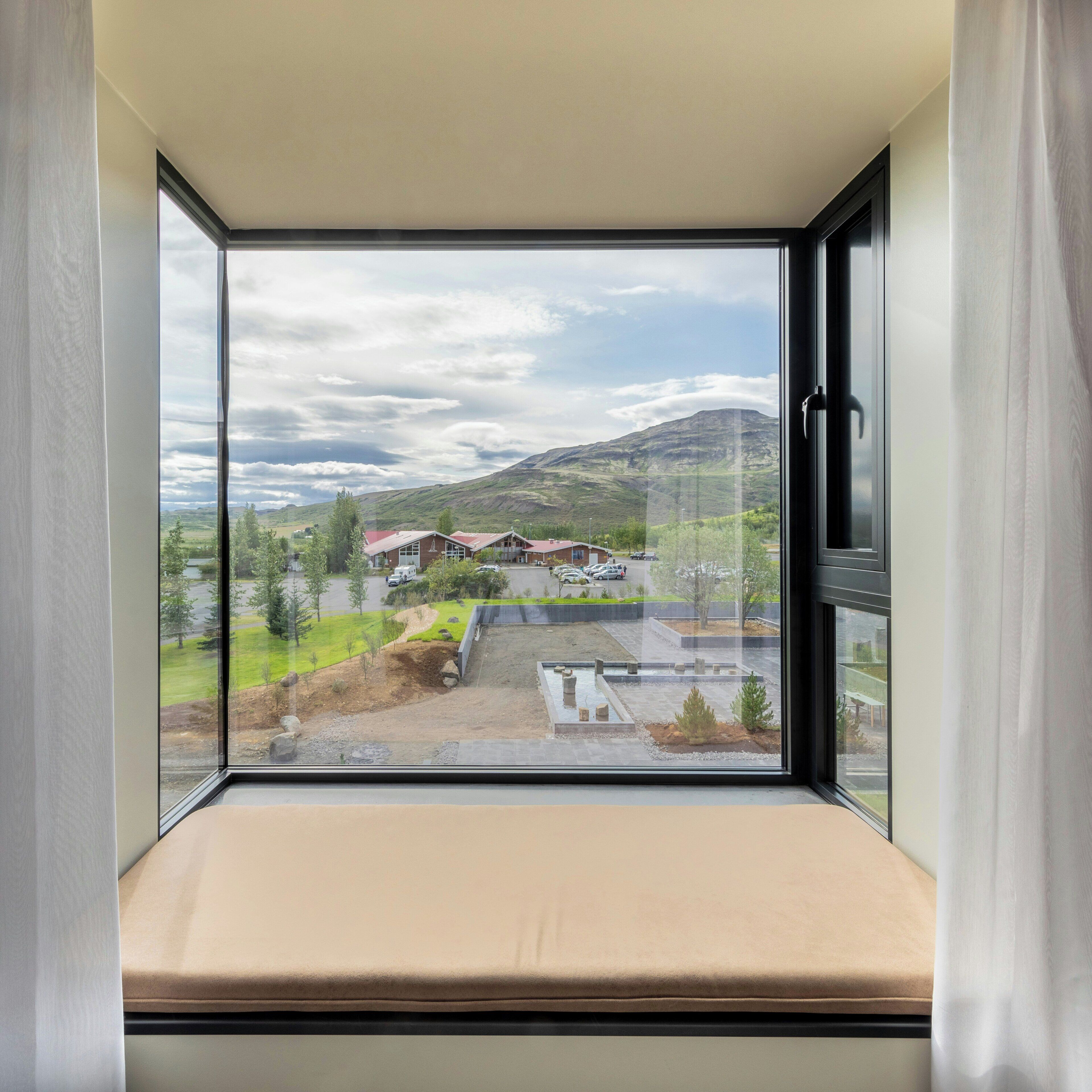 Quarto com uma janela ampla que oferece vista para uma área residencial, um estacionamento e uma montanha.