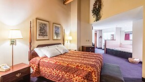 Quarto de hotel com uma cama grande, duas luminárias de cabeceira, um criado-mudo com telefone e um pequeno banco.