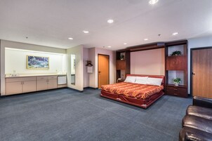 Quarto de hotel com uma cama grande, uma mesa com cadeira, um guarda-roupa e um banheiro pequeno.